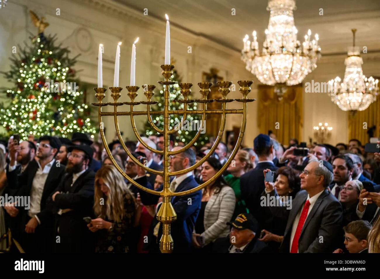 A menorah stands illuminated as attendees gather during a Hanukkah ...