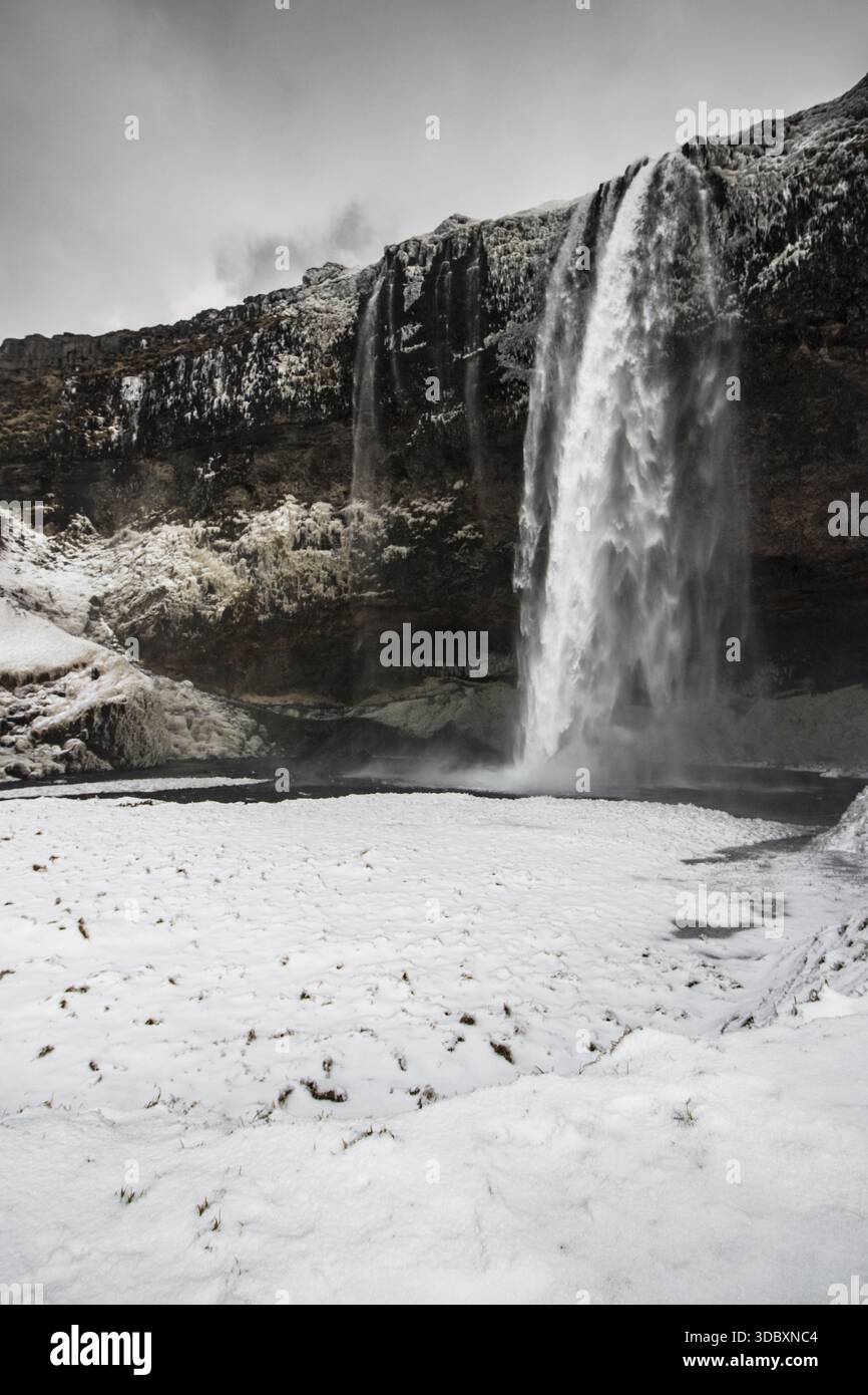 View of cascading water plummets from rugged cliffs into an icy pool ...