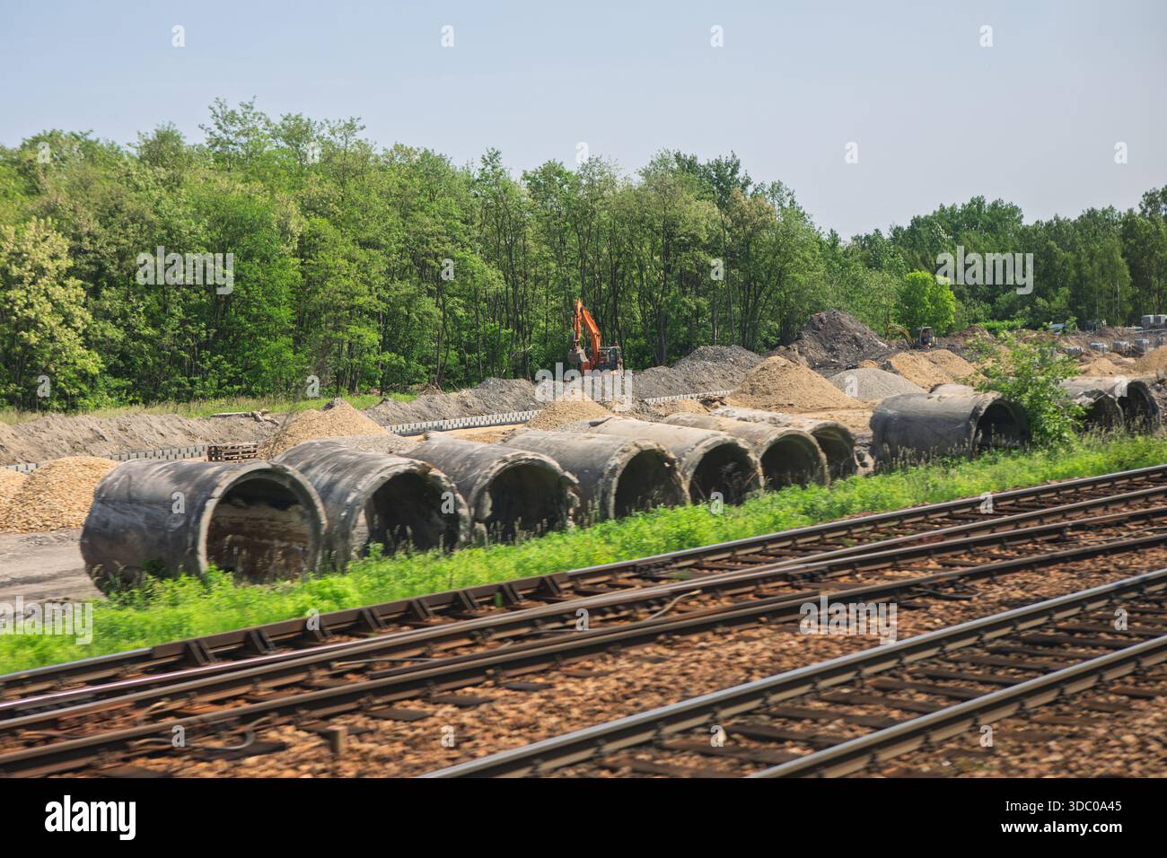 Concrete pipes and gravel piles line a construction site beside active ...