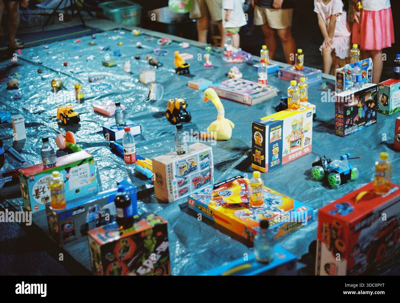 A colorful night-time toy stall, with boxed prizes and plastic bottles ...