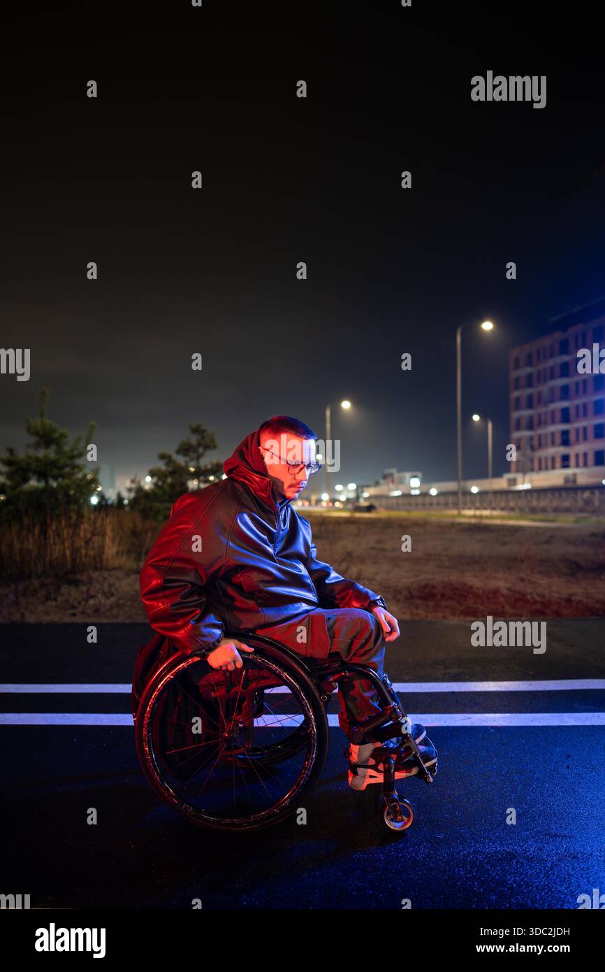 Sad young man with disability in wheelchair on pathway in rgb neon ...