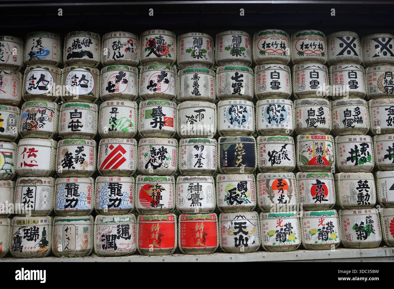 A wall of white sake barrels stacked neatly, each adorned with bold ...