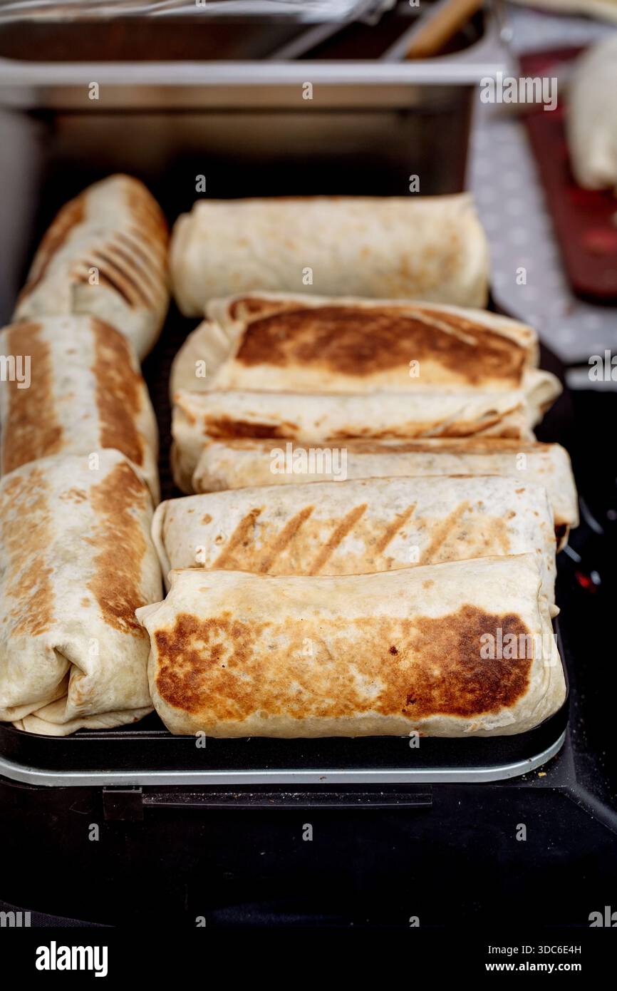 Fresh grilled burritos with golden brown marks cooking on black grill ...