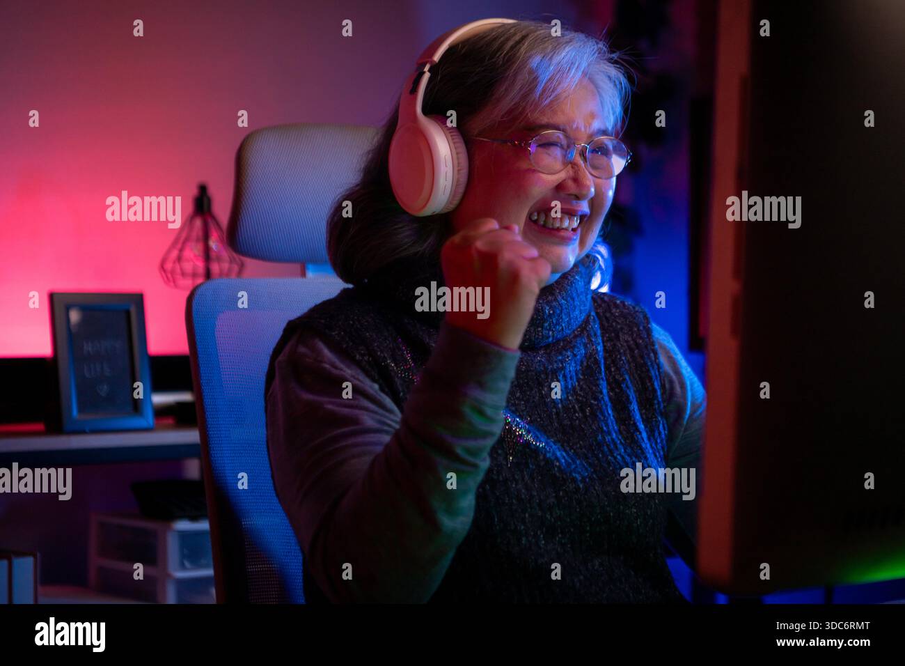Senior woman gamer wearing headphones and playing on a desktop computer ...