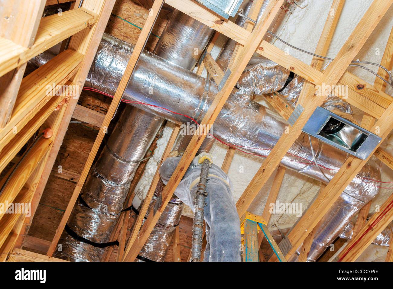 Metal ducts are installed within wooden framing at construction site ...