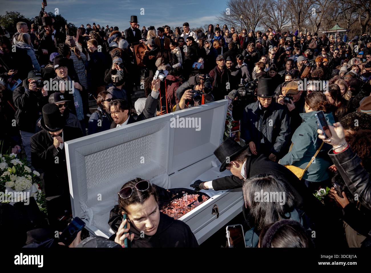 People gather to throw pennies into a casket during a mock funeral for ...