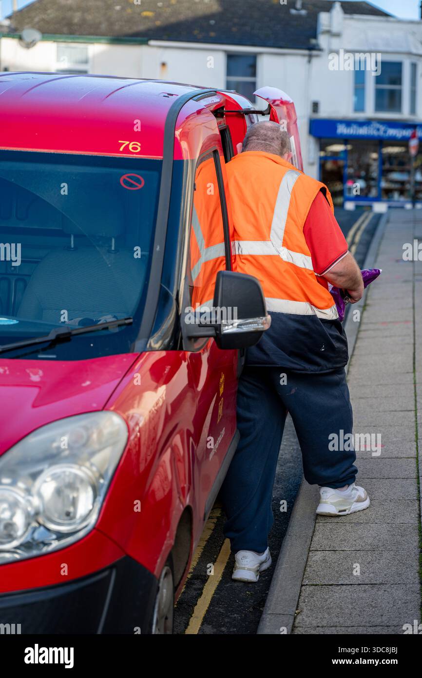 Postman leaning into the back of a post office royal mail van to ...