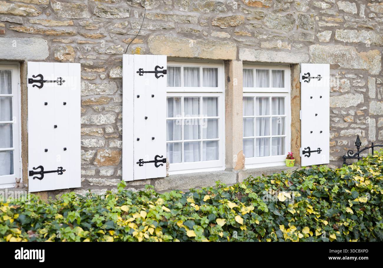 Traditional wooden windows with white shutters on an old stone cottage ...