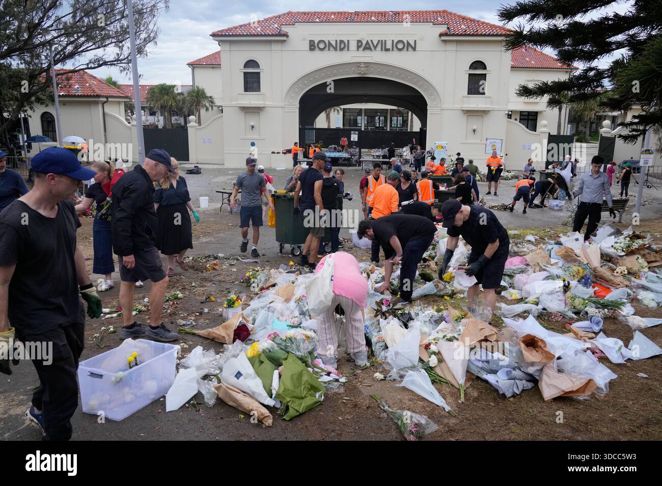 Workers gather floral tributes, messages of support and items left as a ...