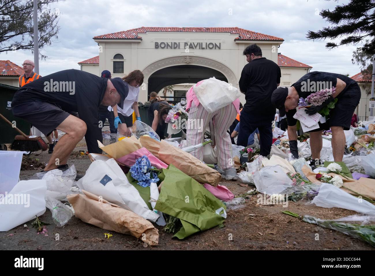 Workers gather floral tributes, messages of support and items left as a ...