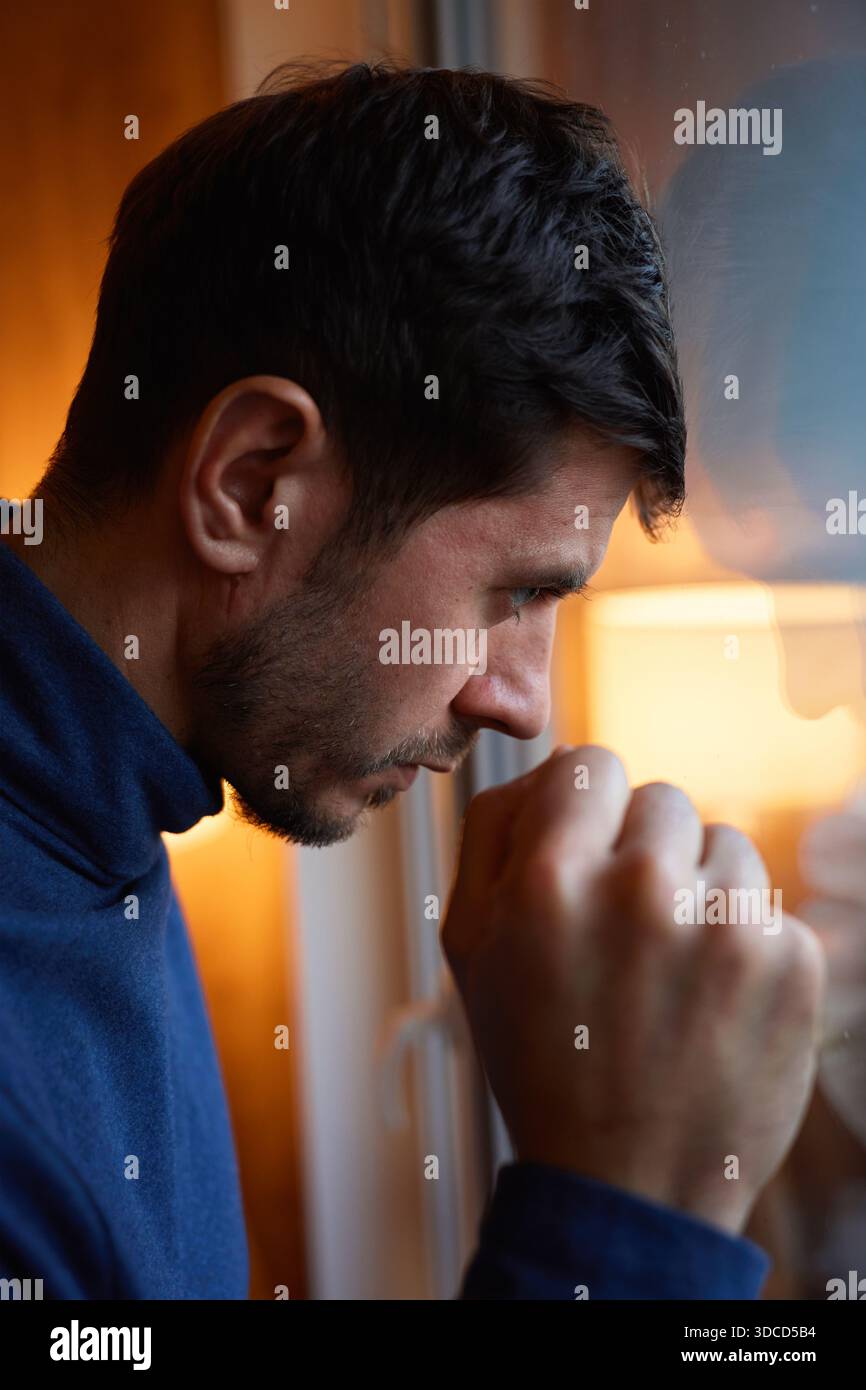 Portrait of worried man leaning on window and looking down with ...