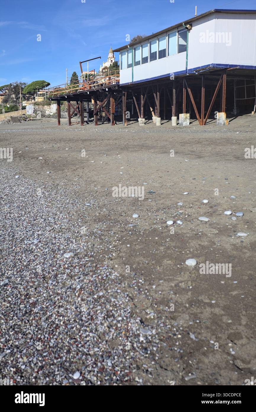 Abandoned resort building on stilts on a beach and next to a stone ...
