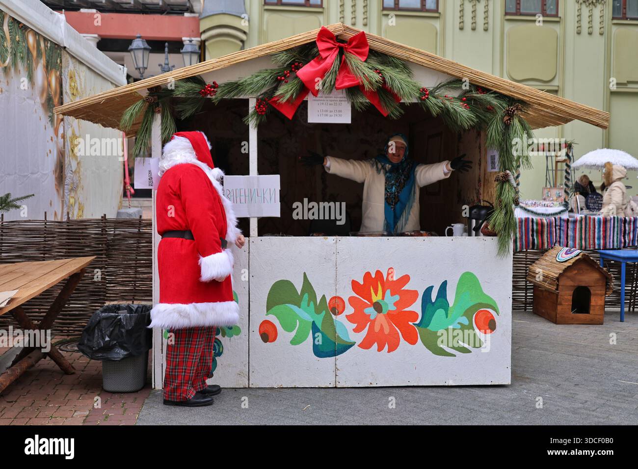 An entertainer dressed as Santa Claus stands by a stall selling ...