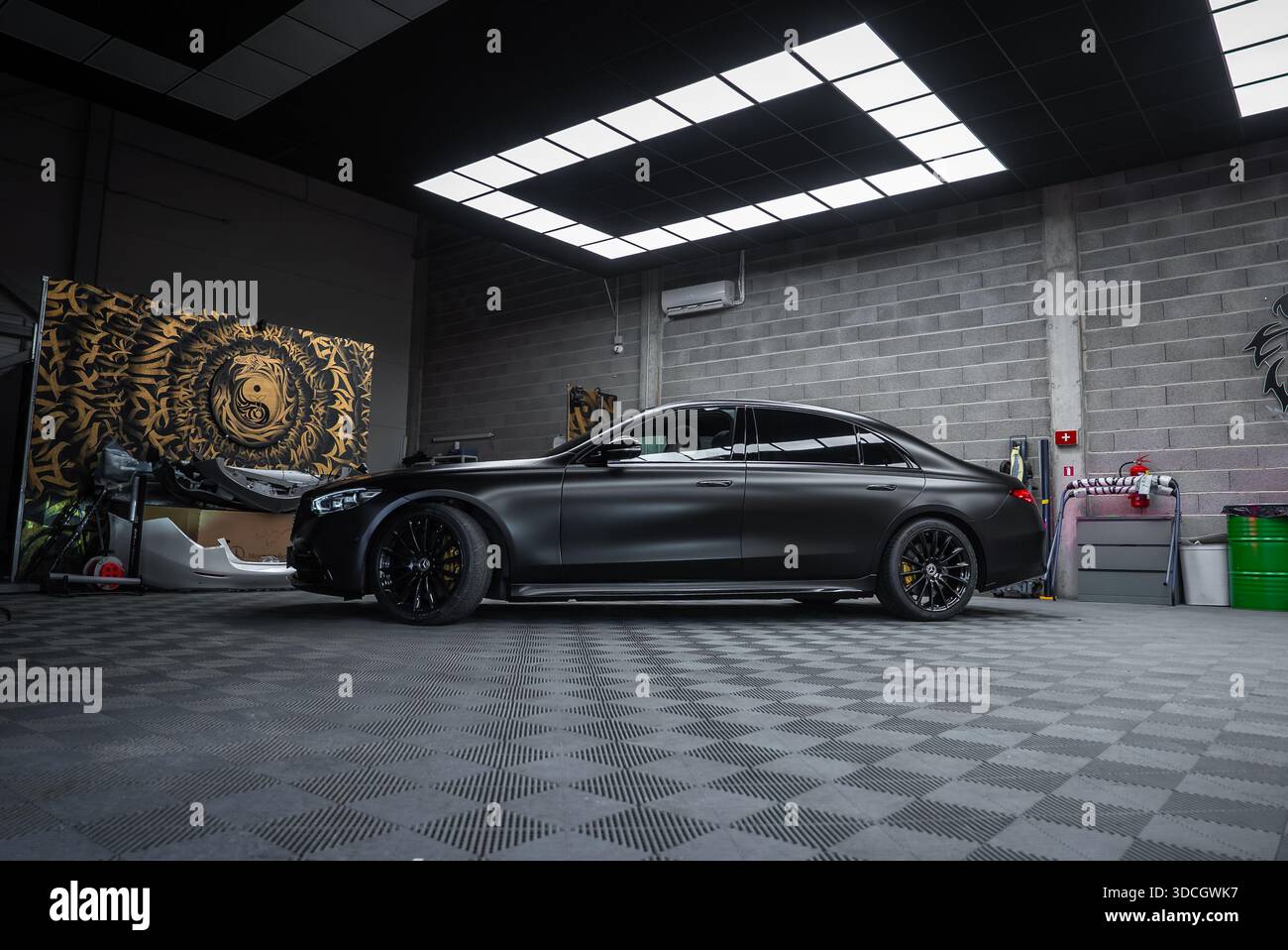 A matte black Mercedes Benz S Class sits in a studio with grid lights ...