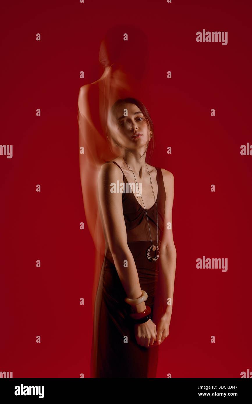 A beautiful woman stands gracefully, with a blurred figure behind her ...