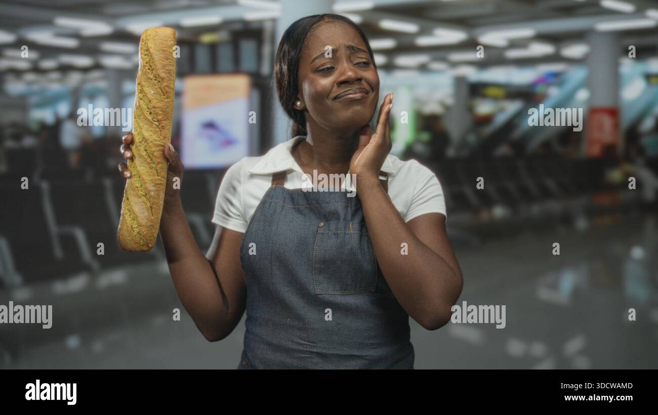 Woman baker in apron holds baguette, touches cheek with a wince in ...
