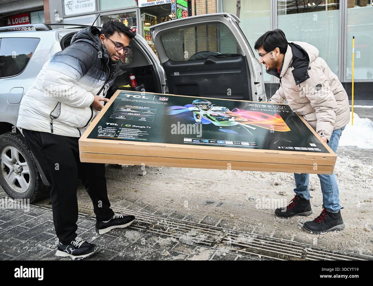 Two men load a large screen television into a car on Boxing Day in ...