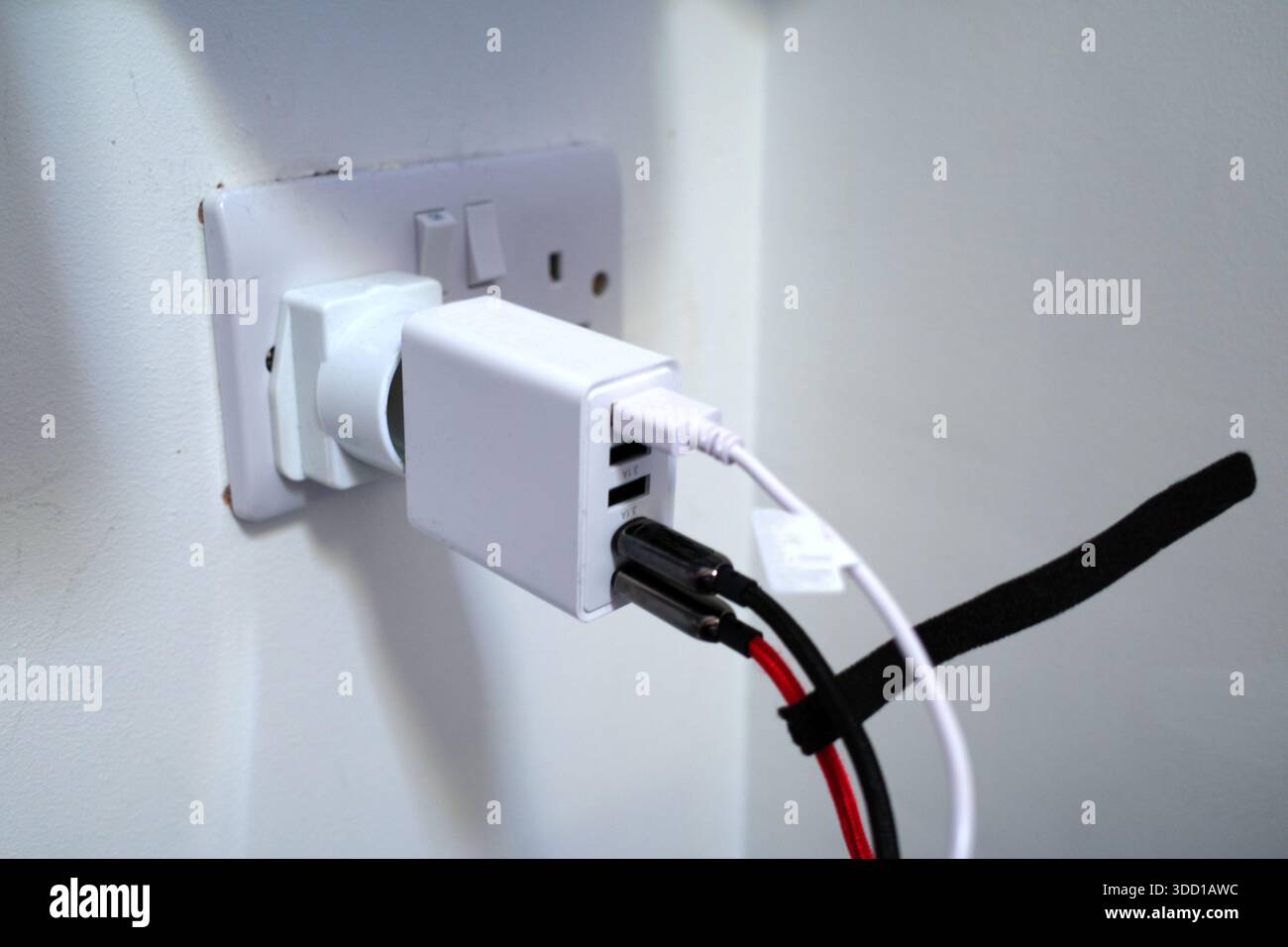 A white electrical adapter is plugged into a wall socket, connected ...