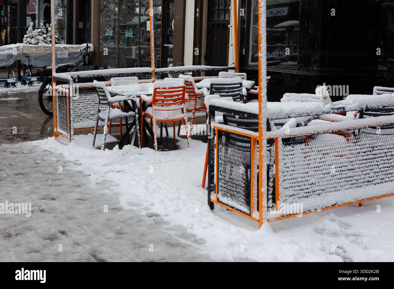 Snow covers tables and chairs outside a restaurant in a city. The scene ...