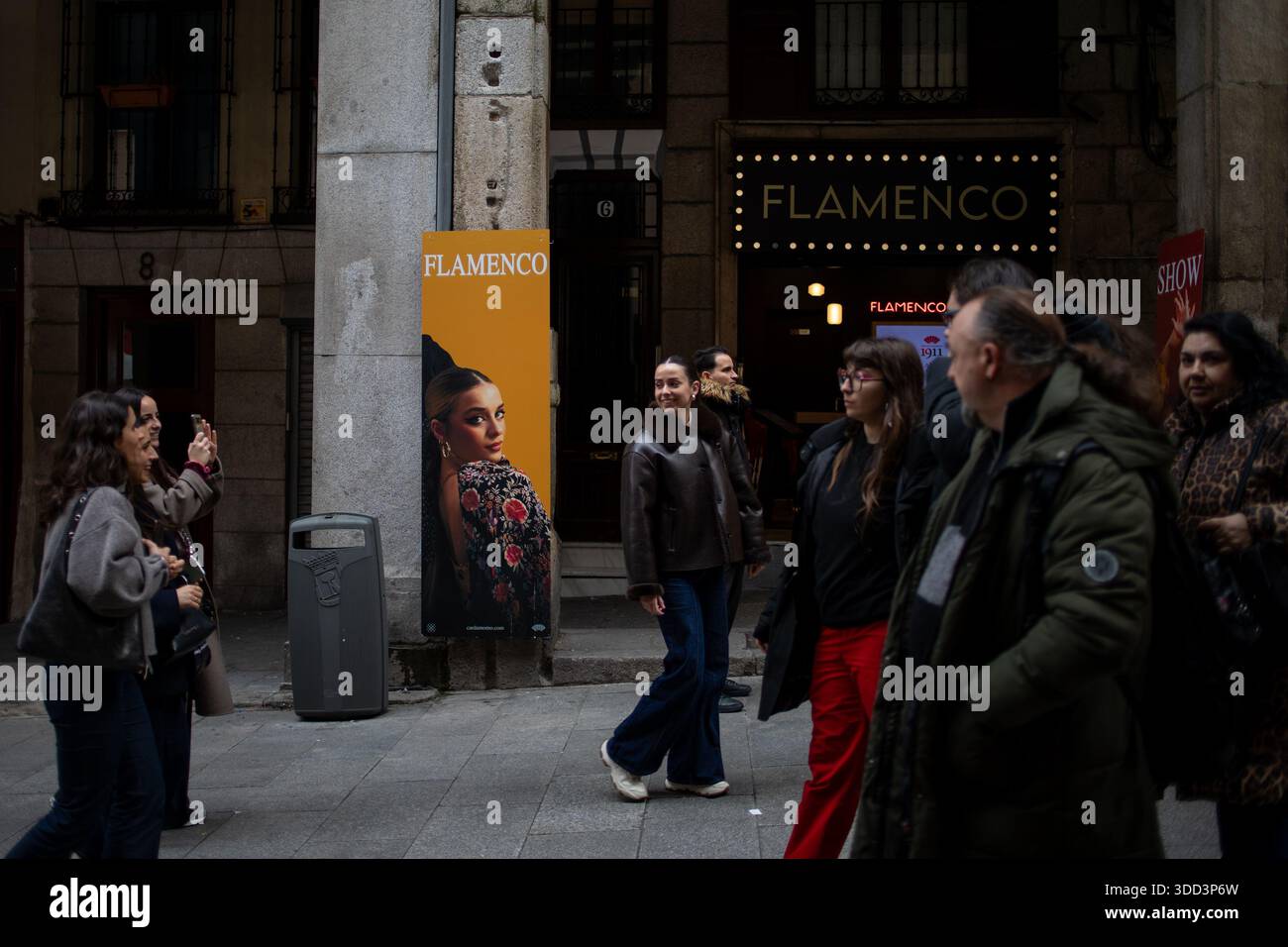 A group of people walk past a sign for a flamenco venue in the center ...