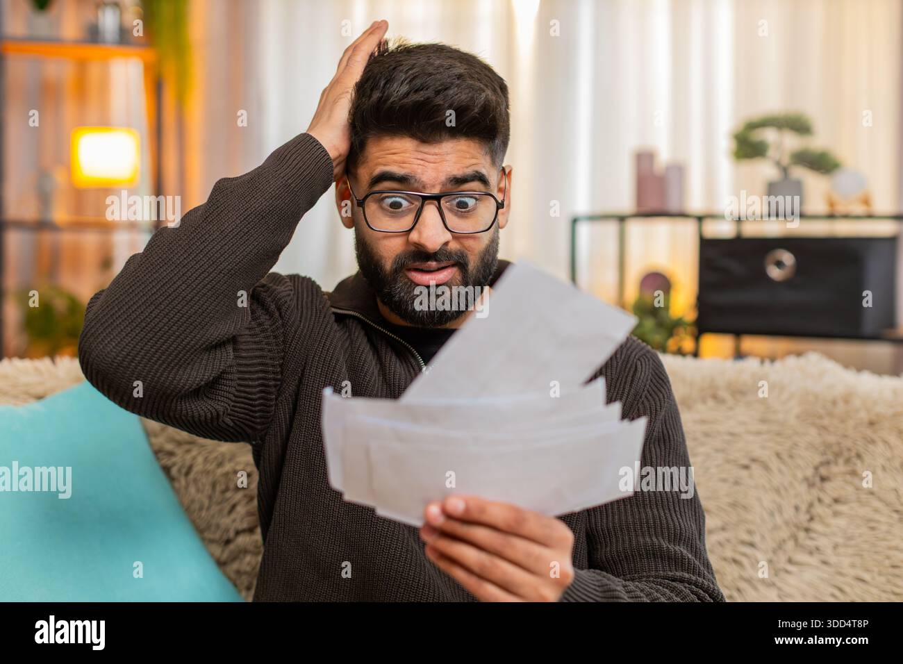 Indian man at home checks bills receipts with tense expression ...