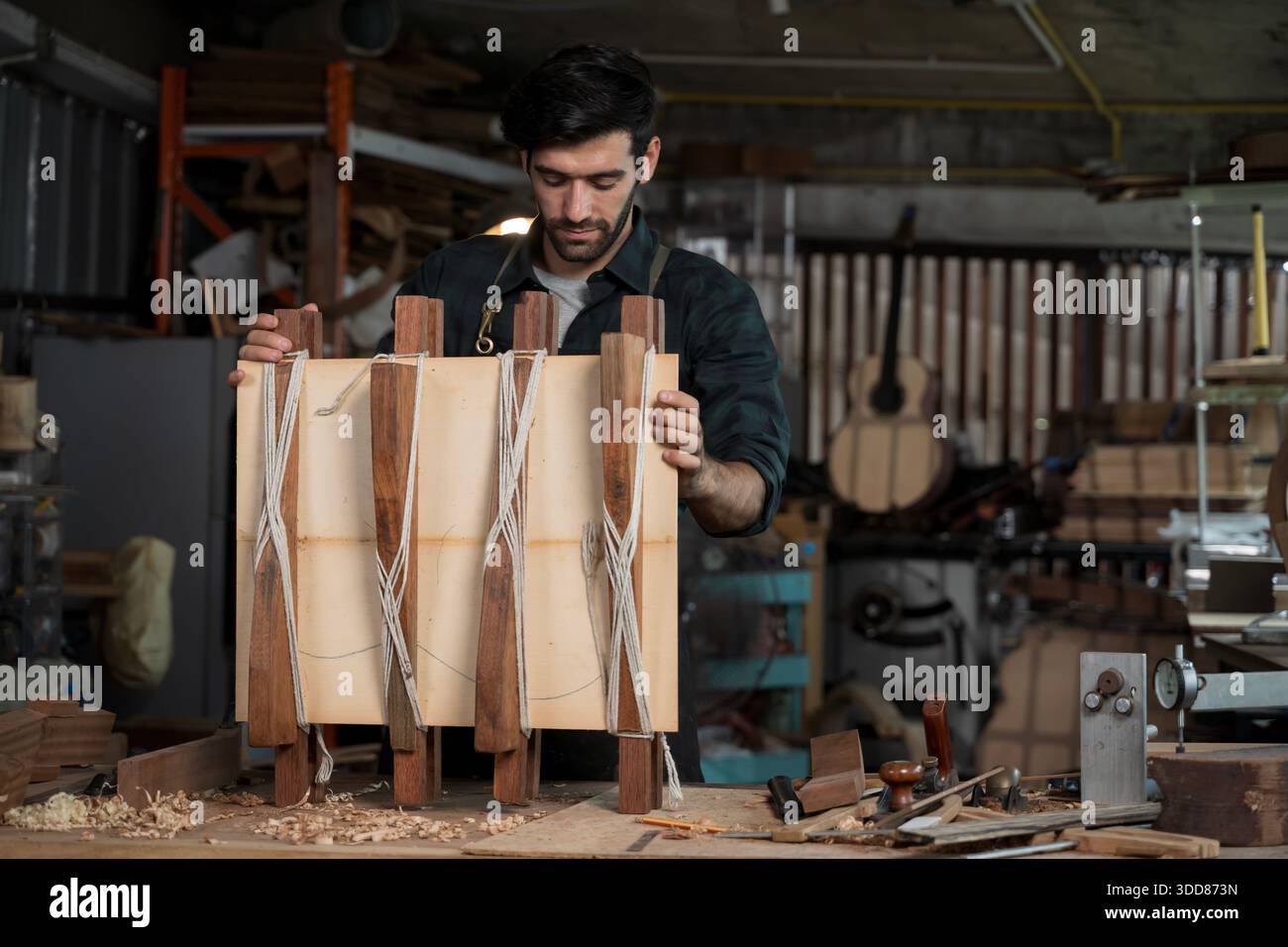 Skilled luthier secures a wooden panel with a clamping jig and ropes on ...
