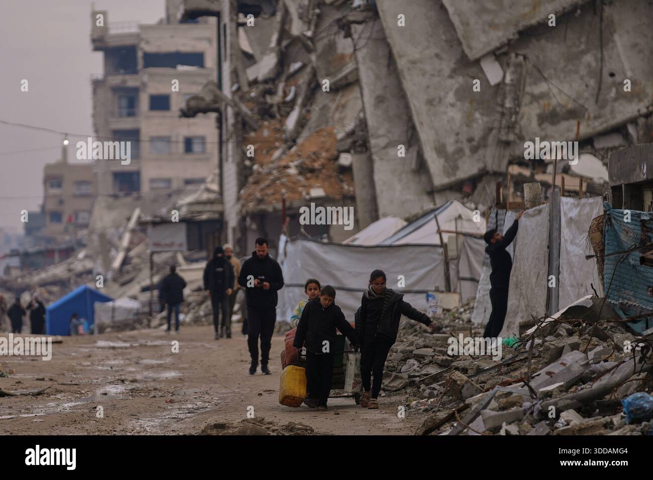 Palestinians walk along a street surrounded by buildings destroyed ...