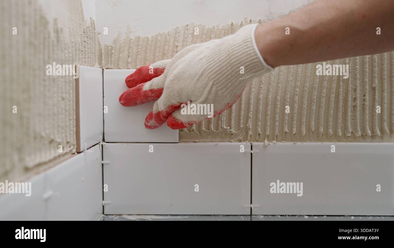 Tiler placing white ceramic tiles on wall with metal profile Stock ...