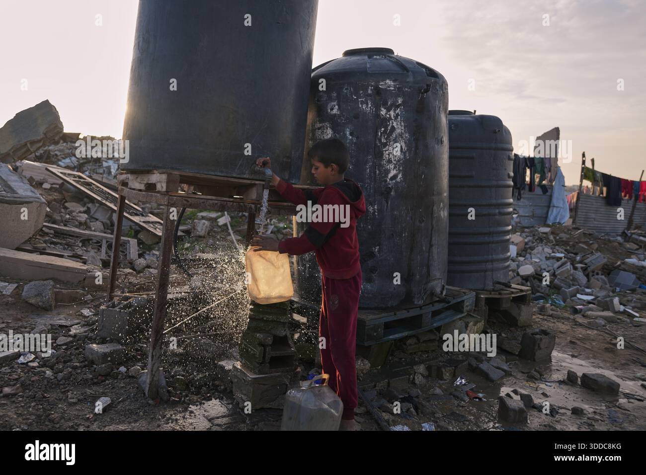 A Palestinian youth collects water from a tank set up next to the ...