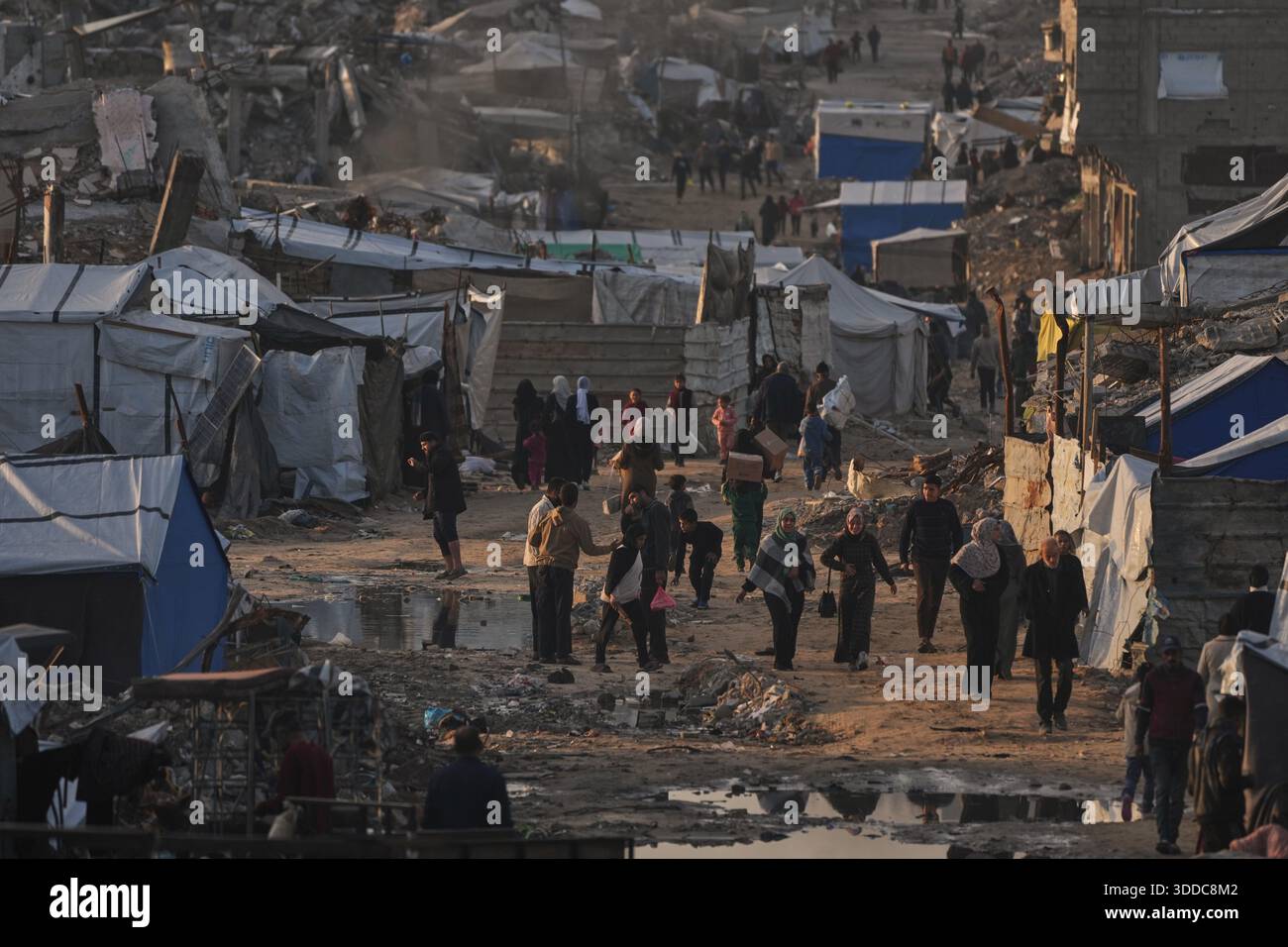Palestinians walk along a street past a tent camp surrounded by ...