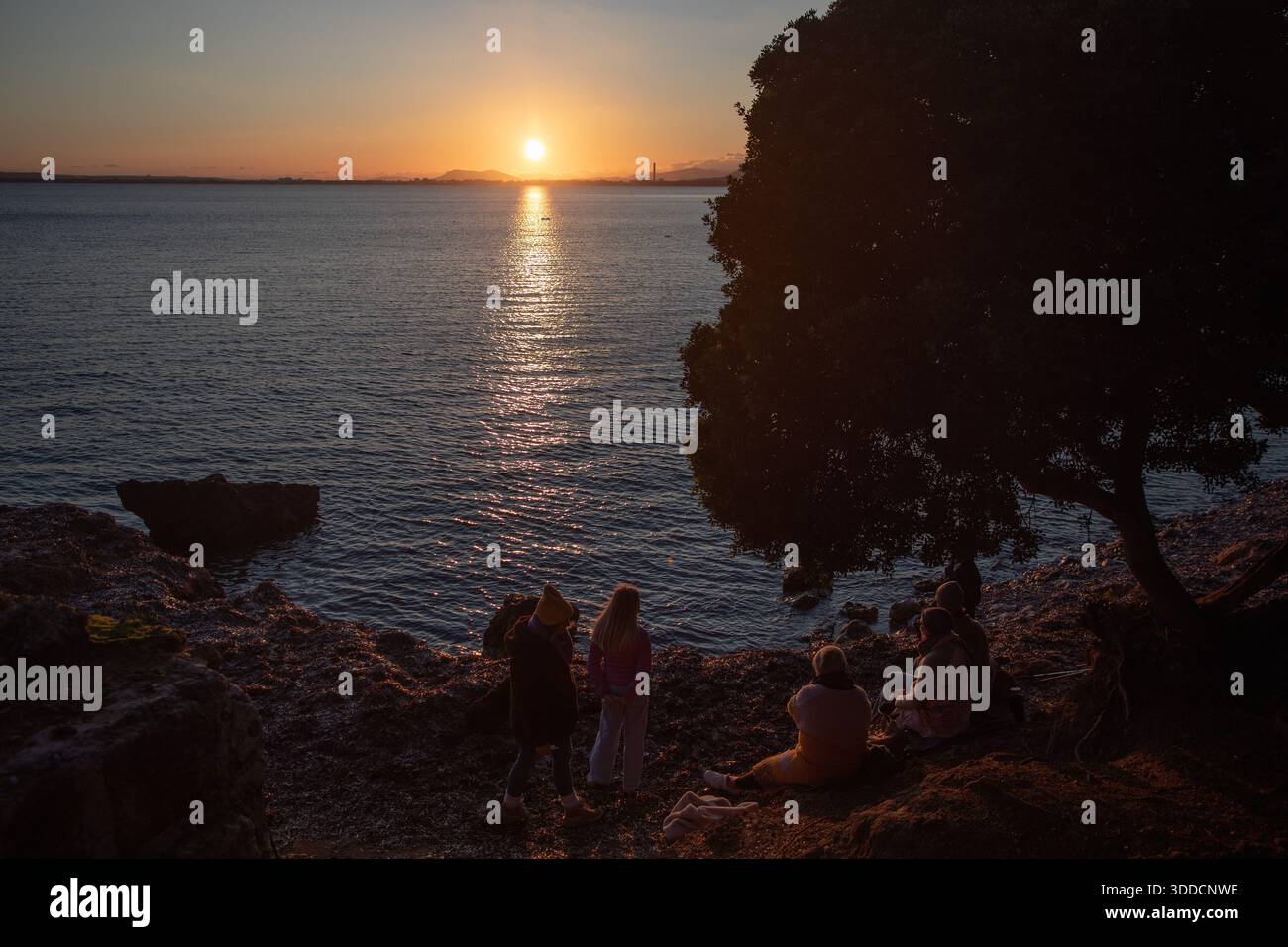 30 December 2025, Spain, Alcudia: People enjoy the sunset by the sea on ...