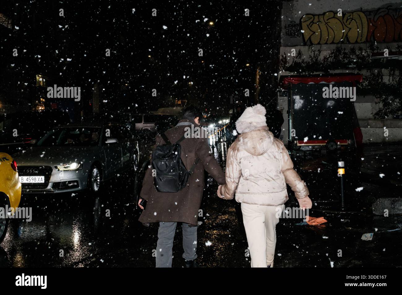 A couple is walking hand in hand under the snow. Snowfall has begun in ...