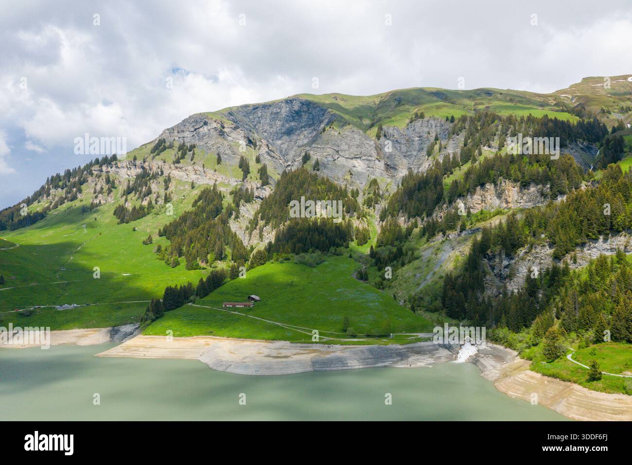 Steep green hills dotted with coniferous trees rise above a calm ...