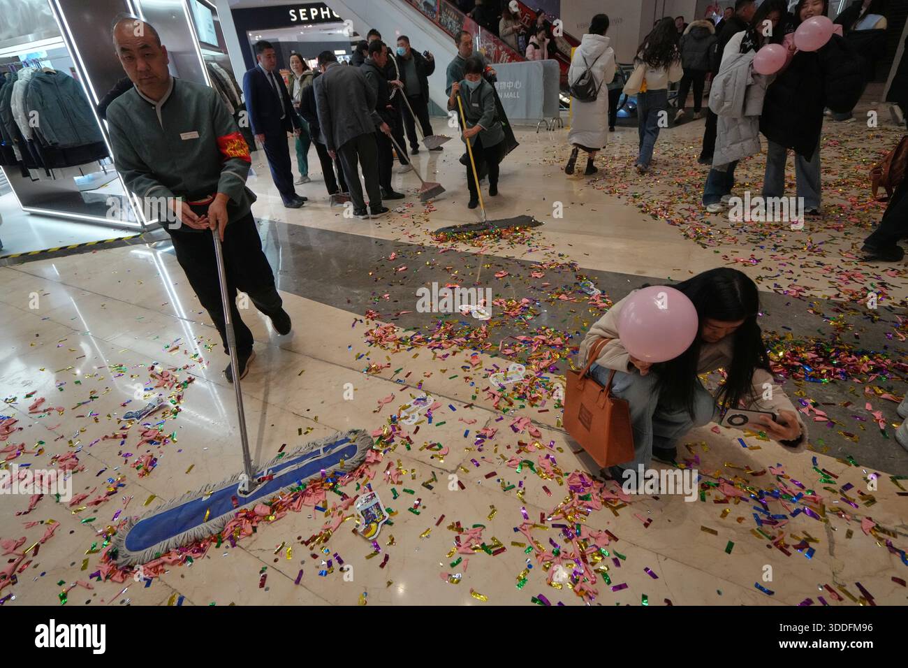A woman films the confetti as workers clean the area after revelers ...