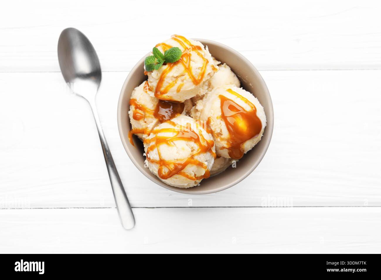 Tasty ice cream with caramel sauce and mint on white wooden table, top ...
