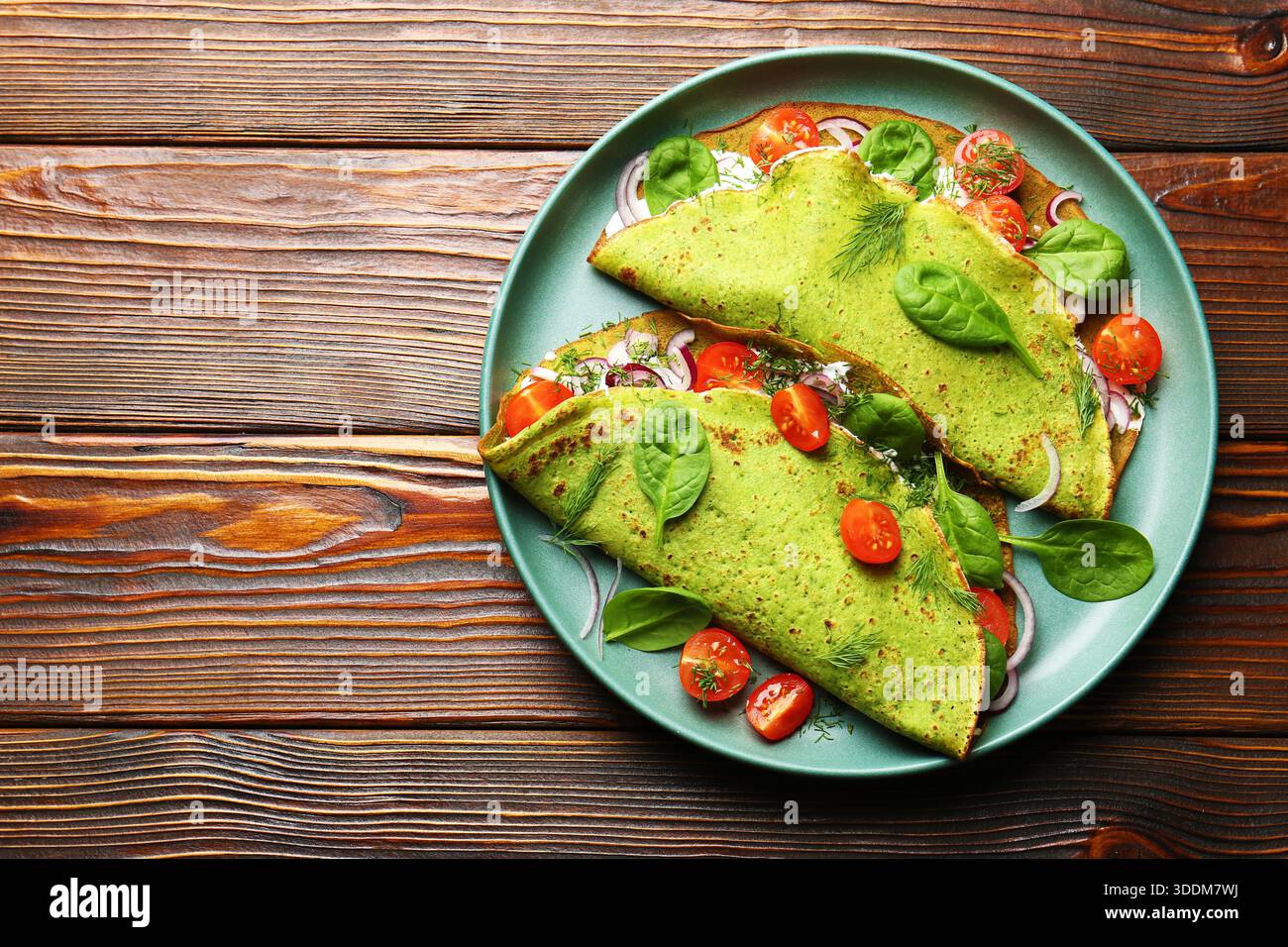 Tasty spinach crepes with tomatoes, onion, sour cream and leaves on ...