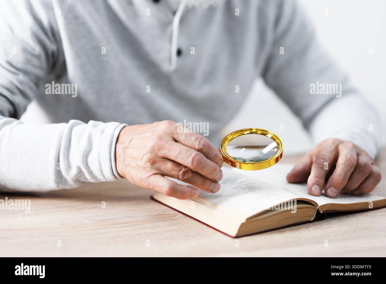 Senior man using magnifying glass while reading book at wooden table ...