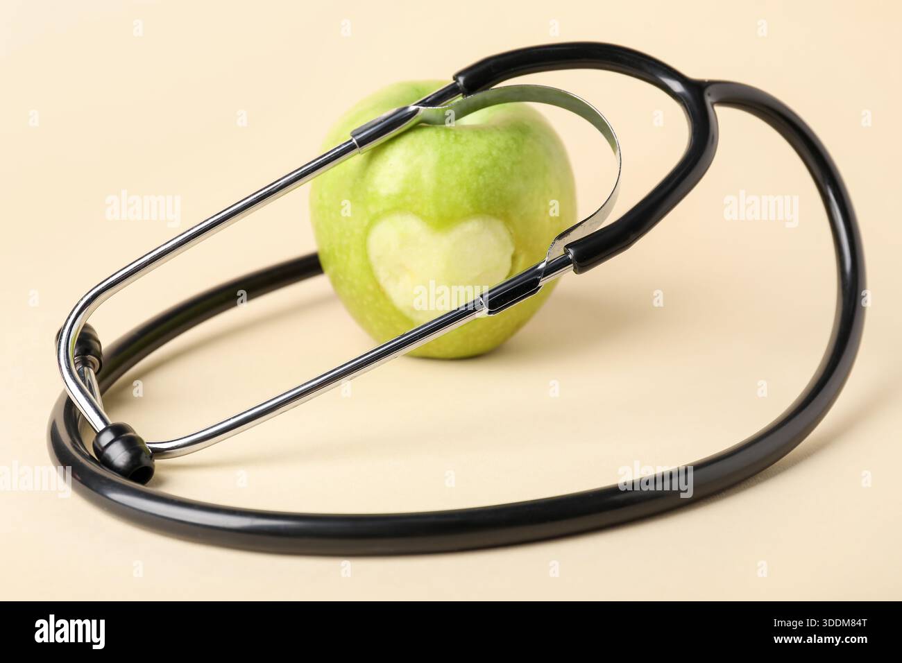 Ripe apple with carved heart and stethoscope on beige background ...