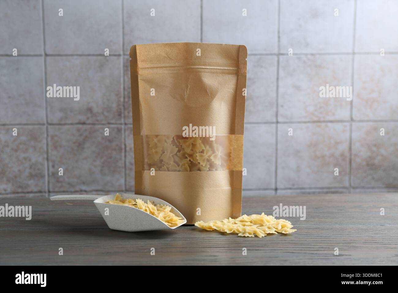 Stand-up pouch with raw pasta on wooden table against tiled background ...