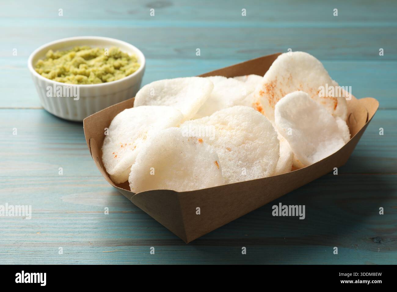 Tasty rice paper chips in takeaway box and wasabi on light blue wooden ...