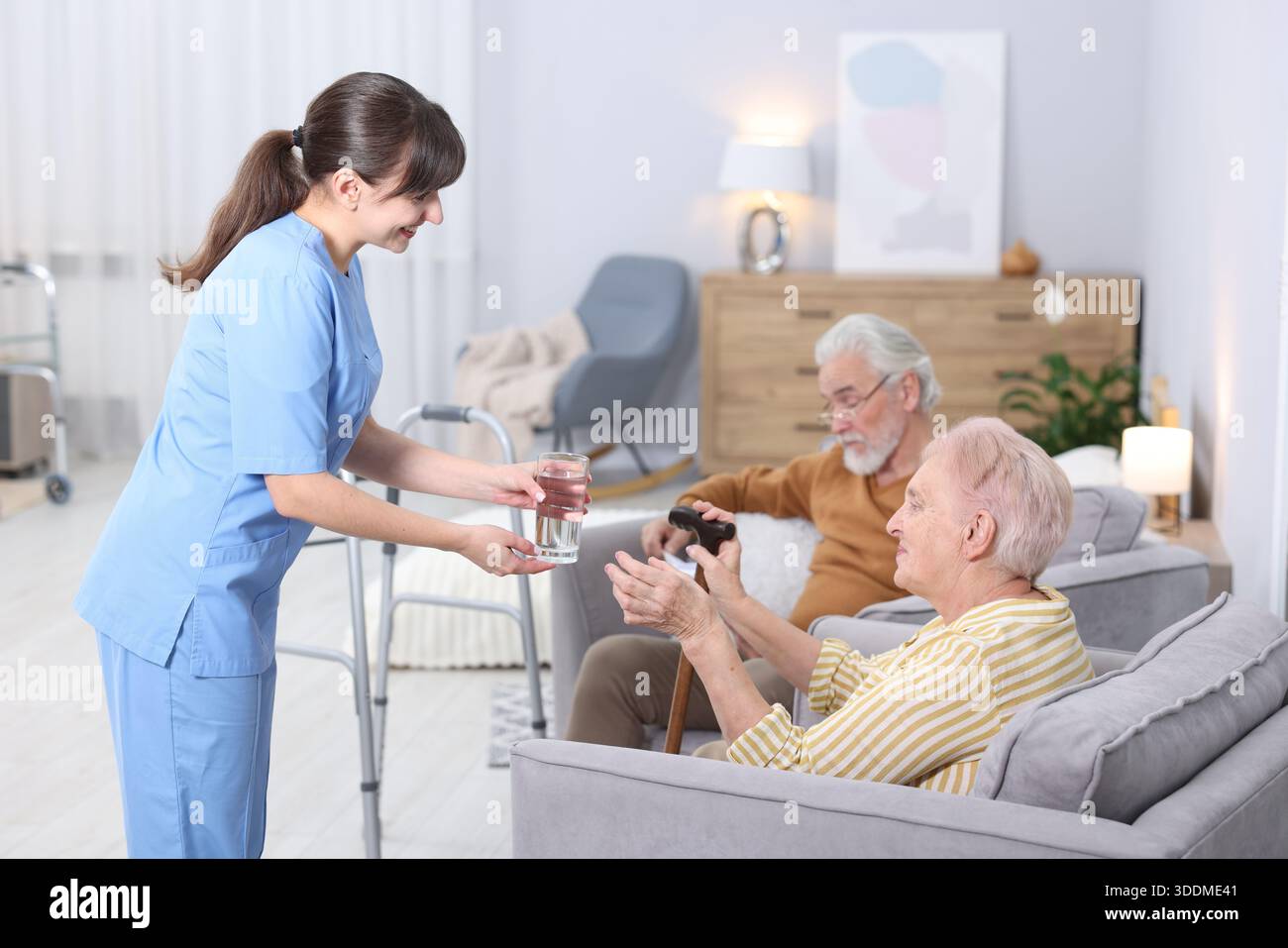 Care worker giving glass of water to senior woman at retirement home ...