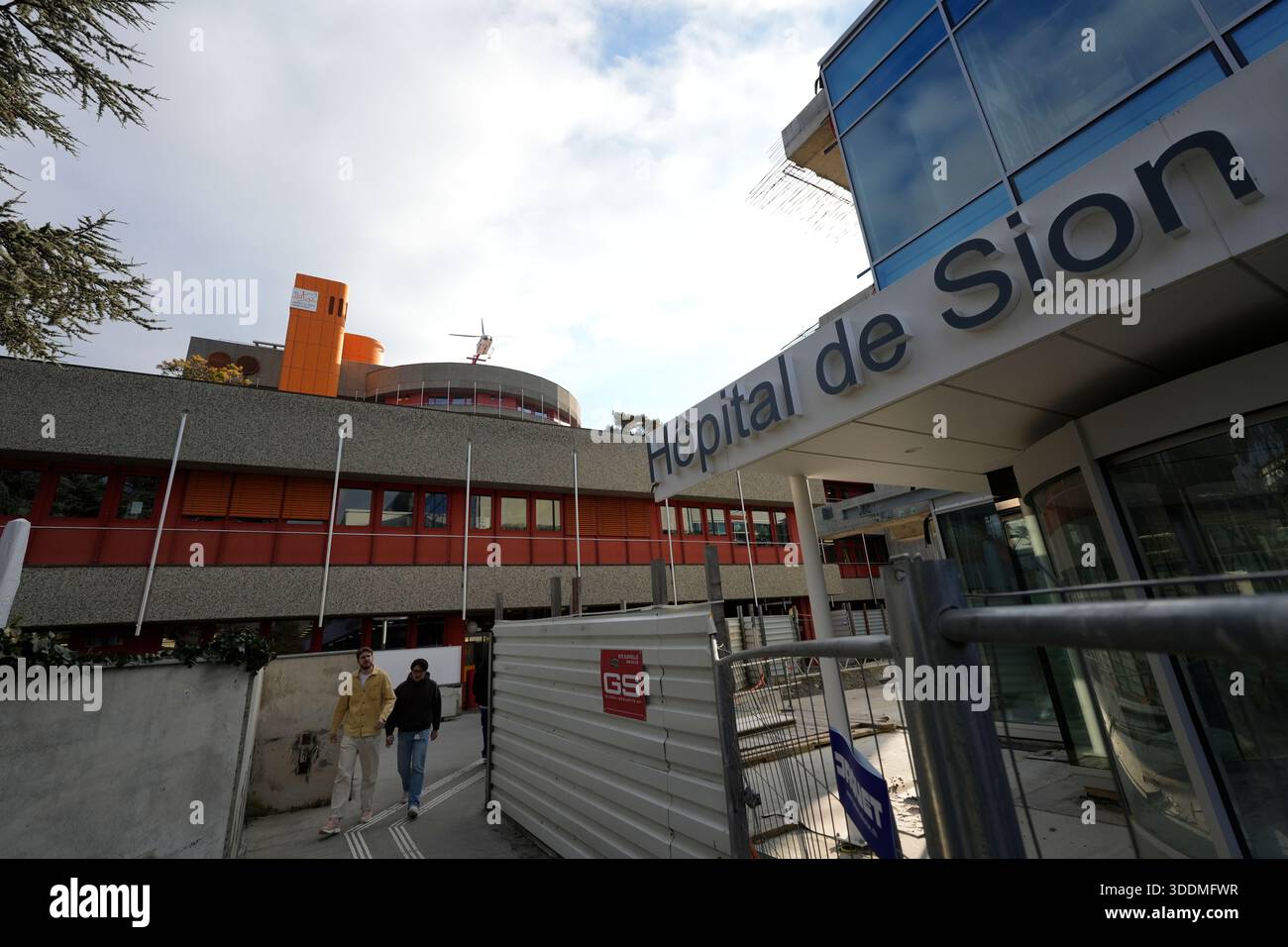 Two men walk outside a hospital as a helicopter takes off in Sion ...
