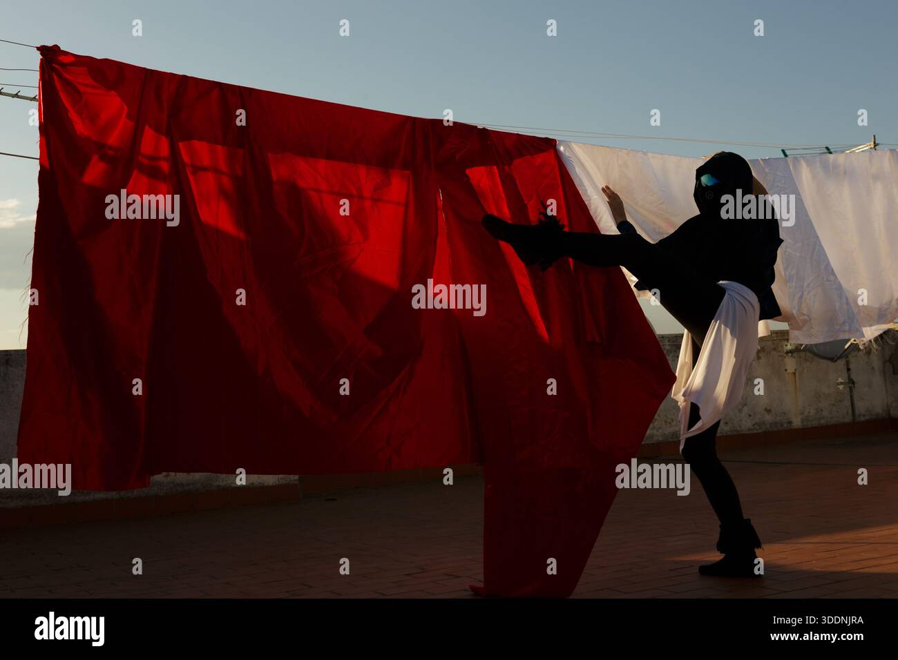 Rooftop figure leaping beside billowing red sheet during golden light ...