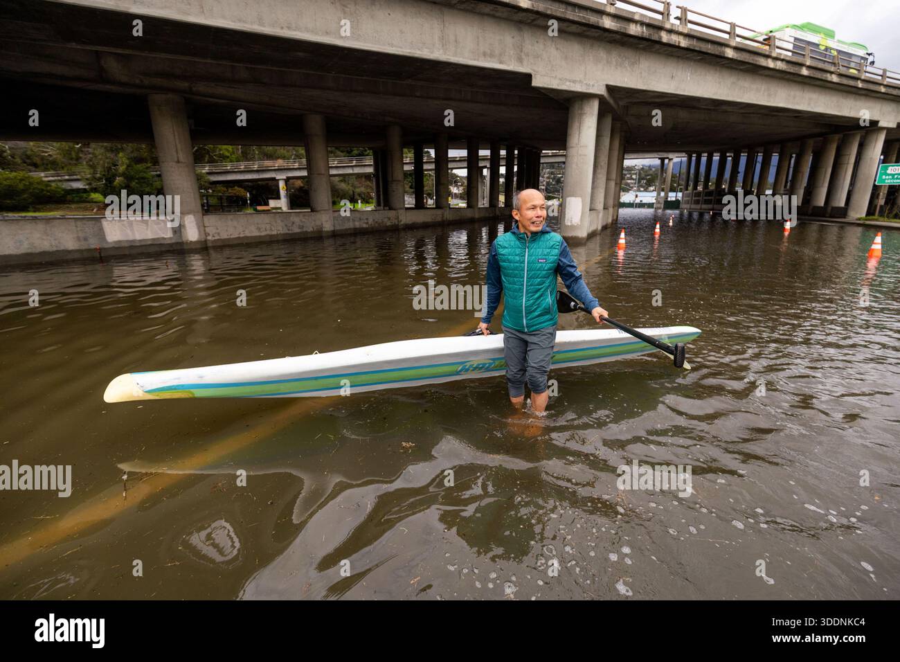 A person paddle boards along a flooded street caused by the king tides ...