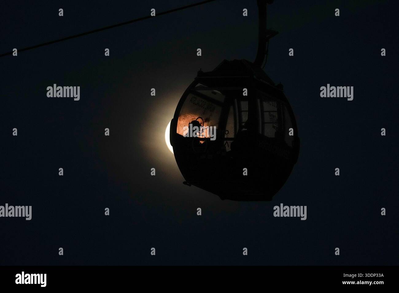 A cable car passenger is silhouetted against a rising super wolf moon ...