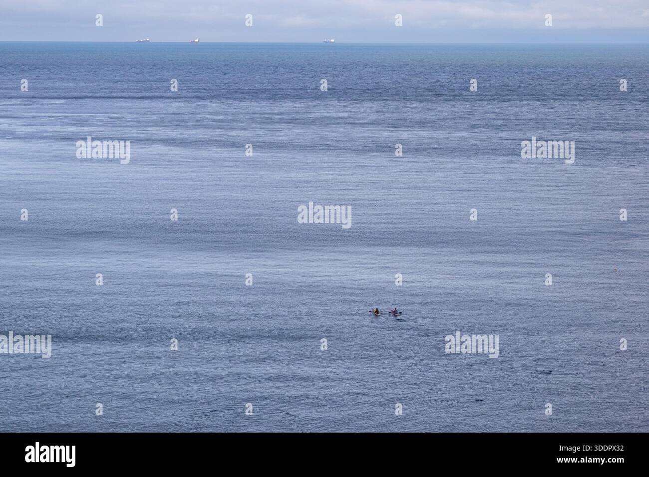 Two kayakers paddling across open sea beneath a distant horizon and ...