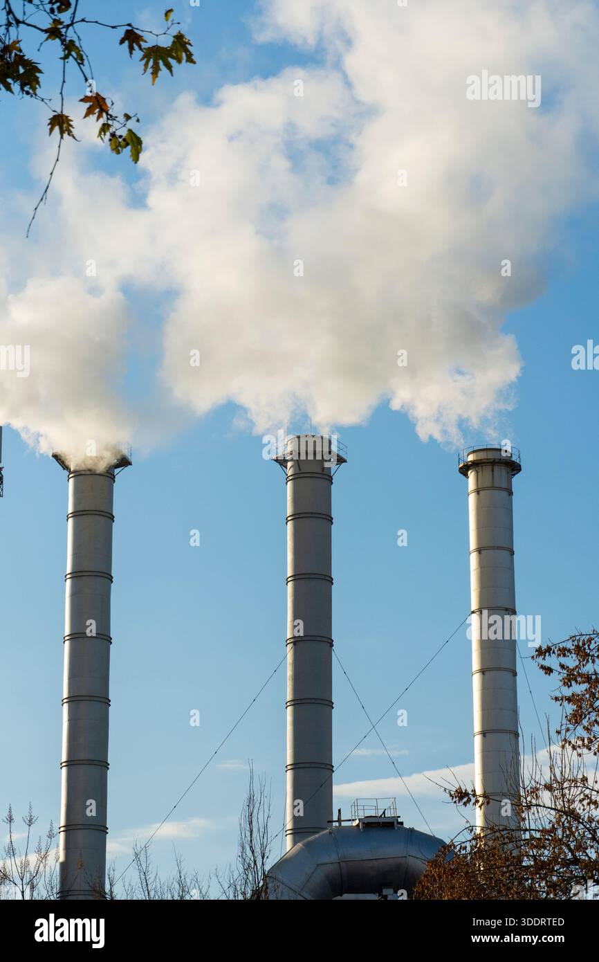 Three smokestacks release thick white smoke into a clear sky ...