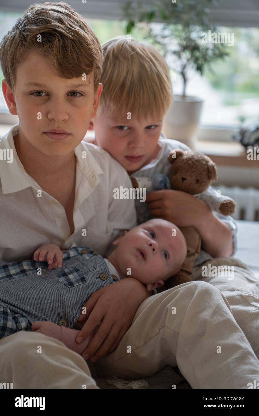 Three brothers sitting together on a bed at home, older siblings gently ...
