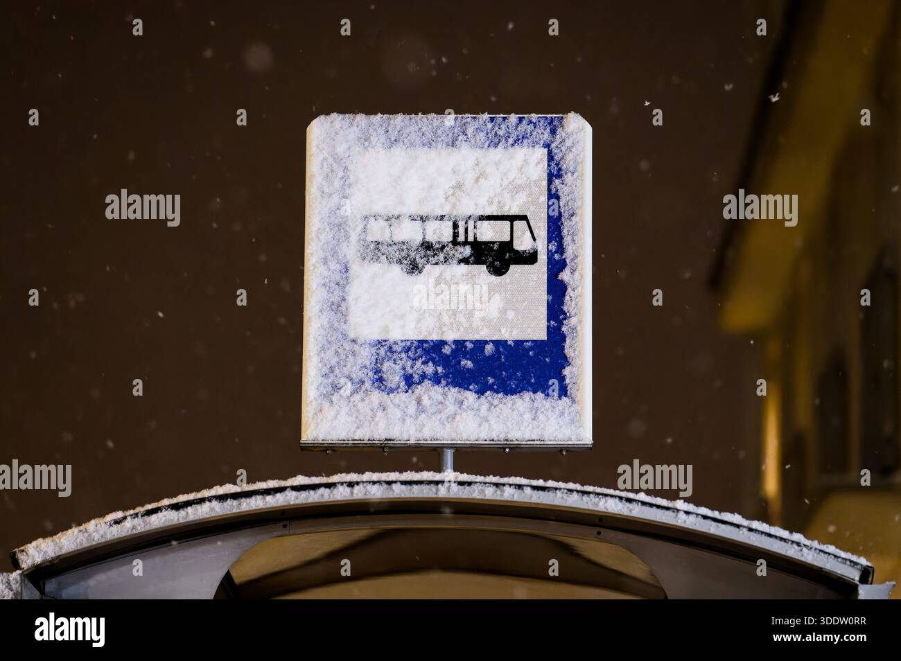 Snow-covered bus stop sign at night with falling snow, winter public ...
