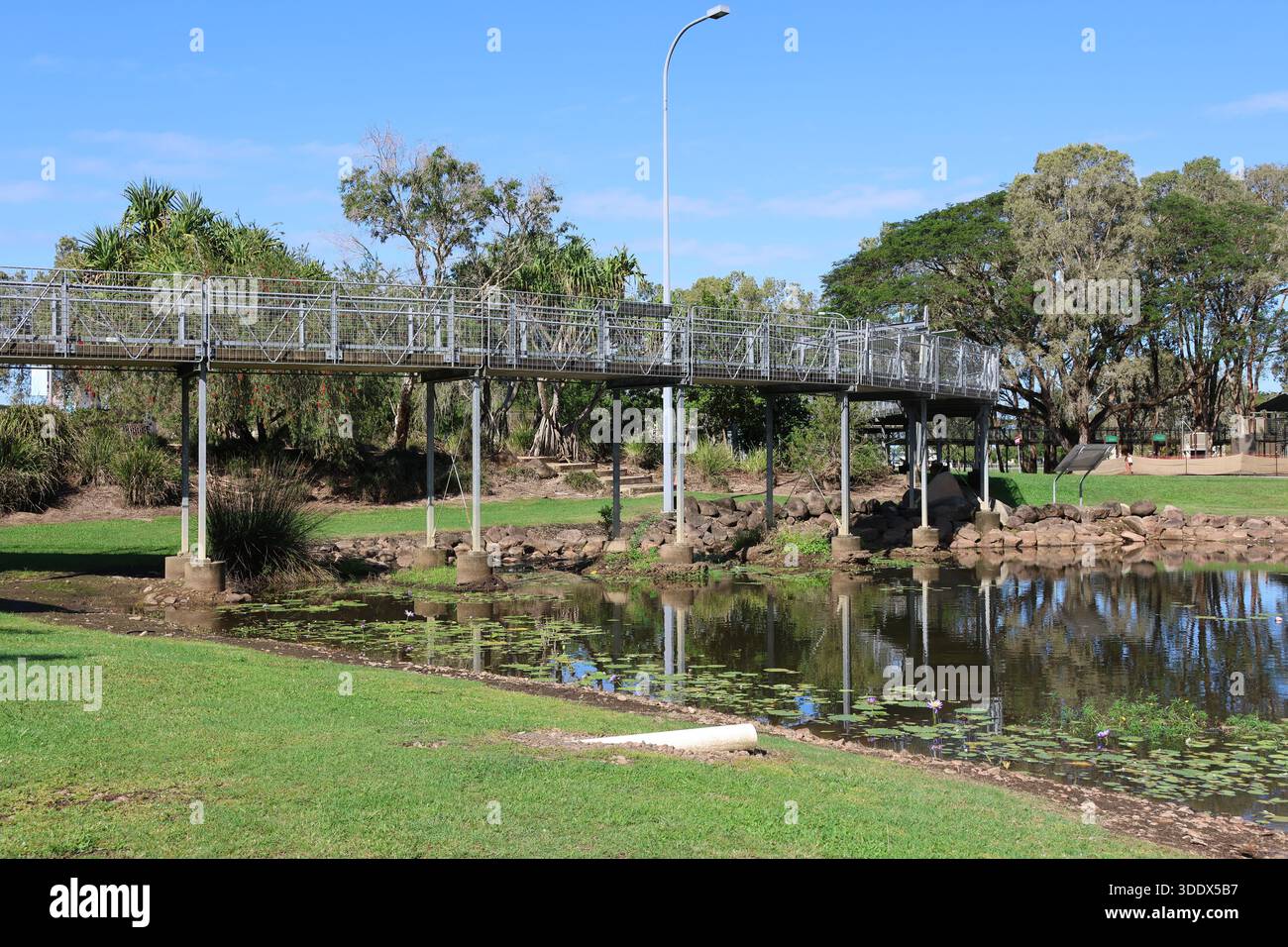 Quiet park scene with a raised pedestrian bridge crossing over a small ...